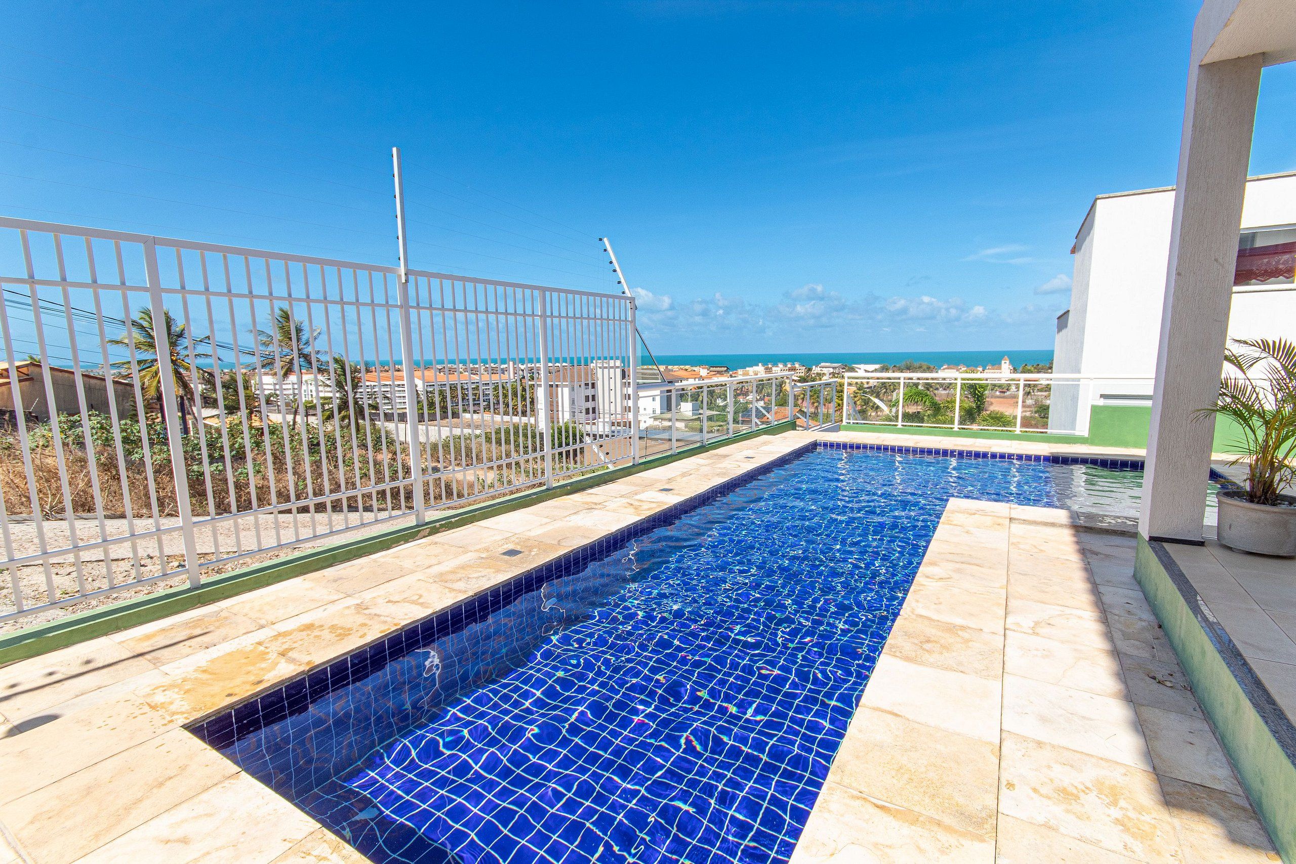Piscina com vista para o oceano, cercada por uma grade e um edifício.