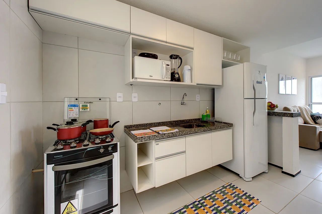 Uma cozinha compacta com armários brancos, forno embutido, micro-ondas e frigorífico.