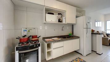 Uma cozinha compacta com armários brancos, forno embutido, micro-ondas e frigorífico.