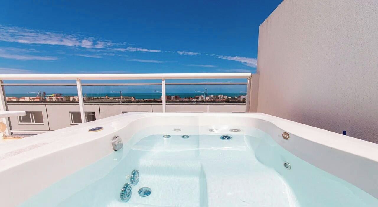 Banheira de hidromassagem em varanda com vista desimpedida para o mar e edifícios ao fundo.