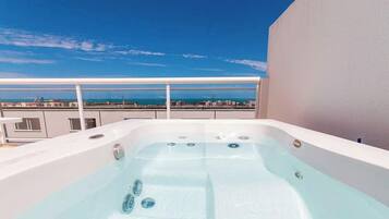 Banheira de hidromassagem em varanda com vista desimpedida para o mar e edifícios ao fundo.