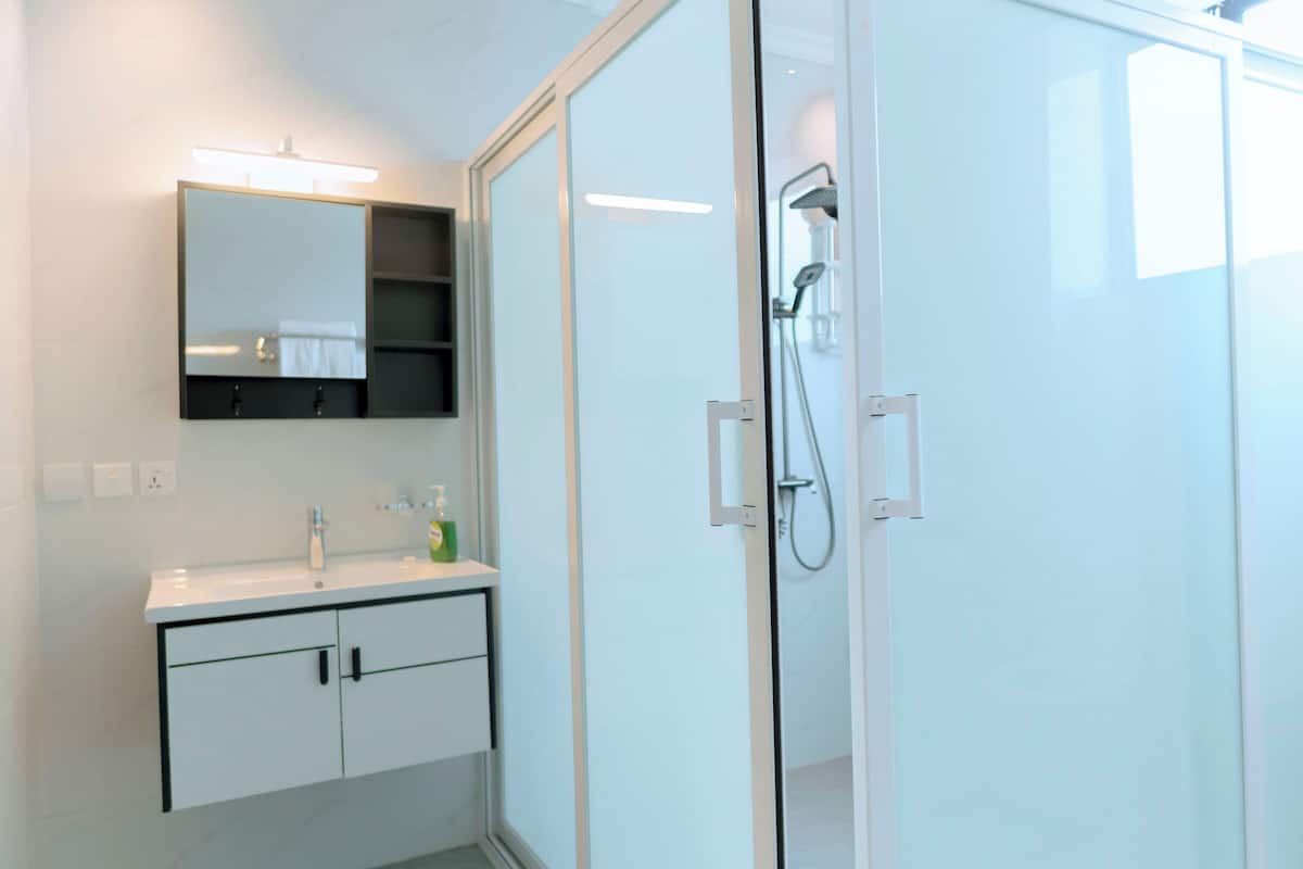 Um banheiro moderno com toucador branco, espelho e área de chuveiro com box de vidro.