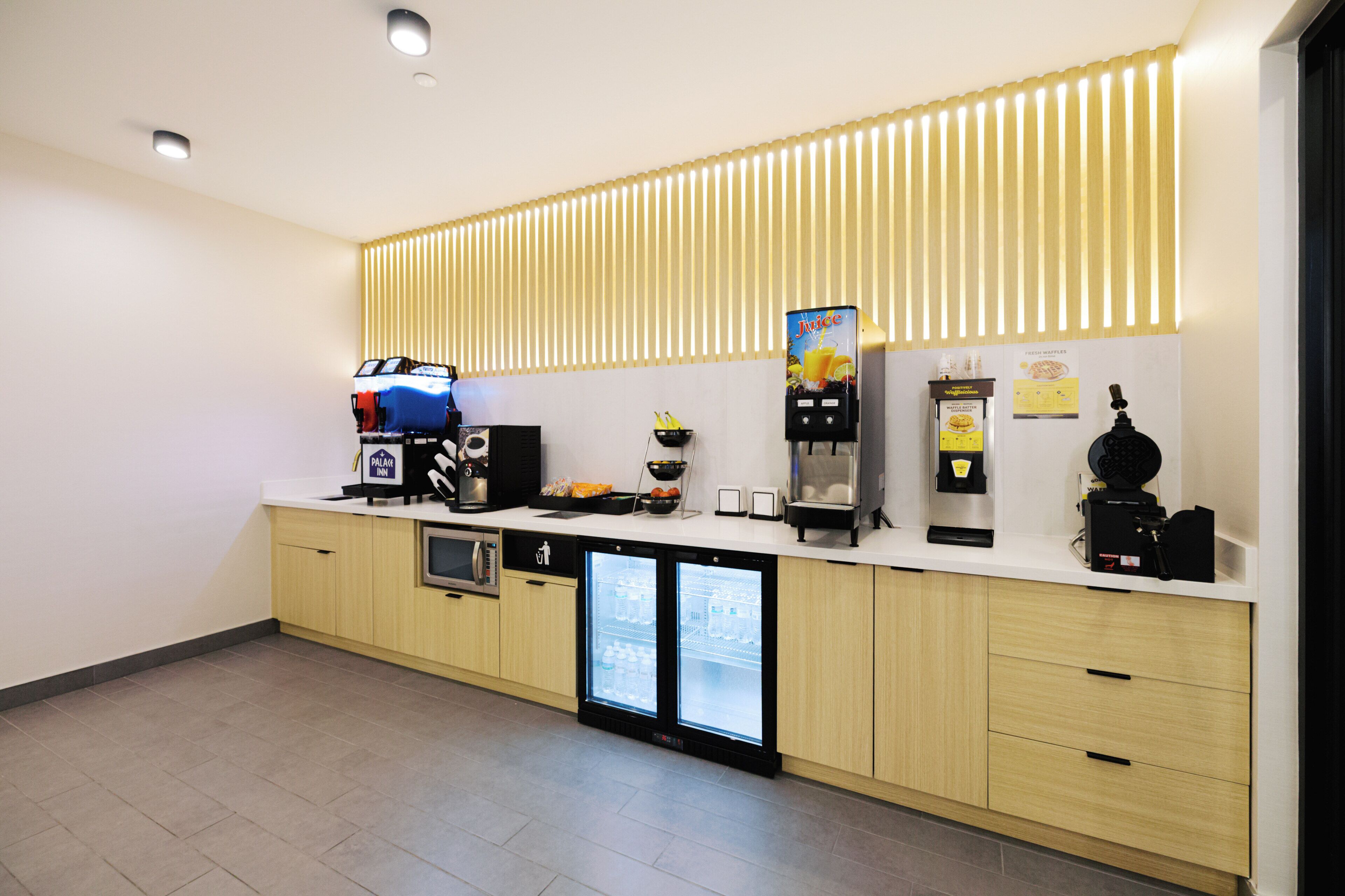 Uma cozinha compacta moderna com cafeteira, mini-geladeira, micro-ondas e dispensador de bebidas.