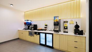 Uma cozinha compacta moderna com cafeteira, mini-geladeira, micro-ondas e dispensador de bebidas.