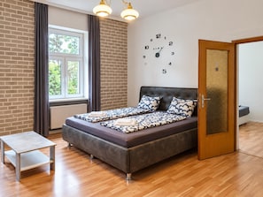Quarto moderno com uma cama grande, uma mesa pequena, uma janela com cortinas e um relógio de parede.