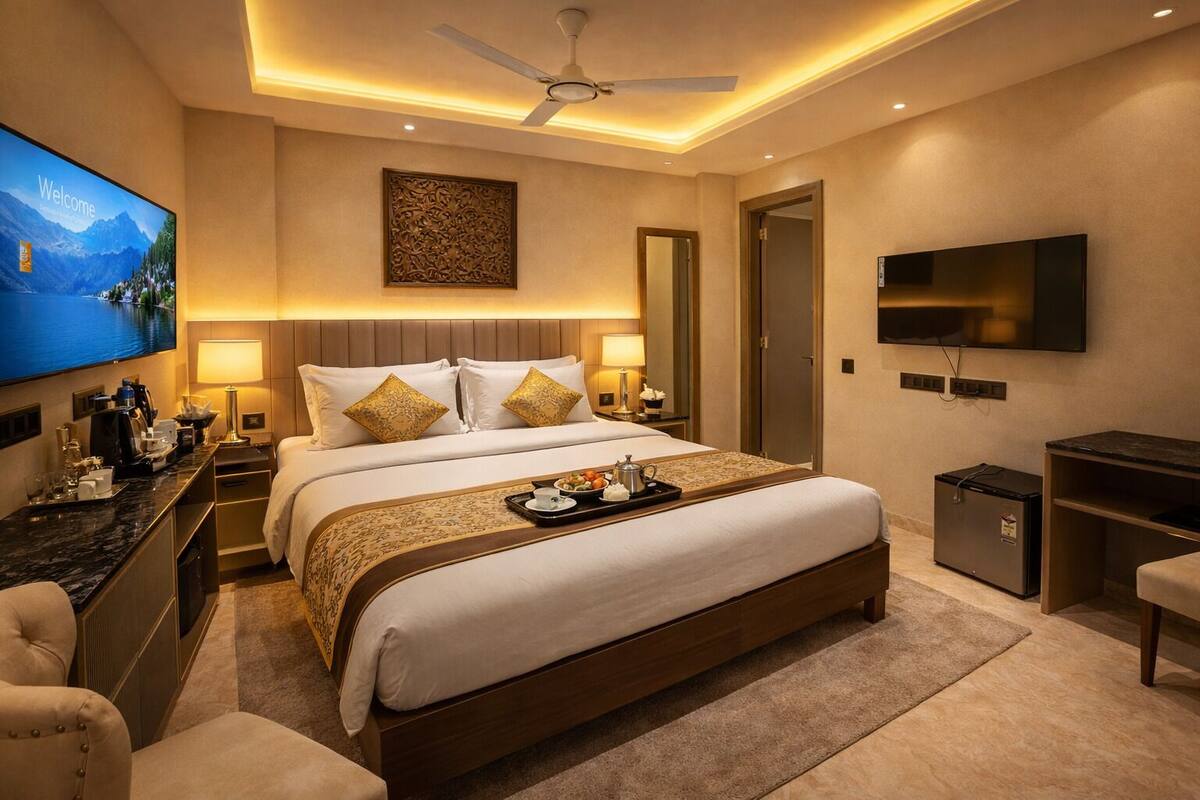 Quarto de hotel espaçoso com uma cama grande, mesas de cabeceira, uma escrivaninha, televisão e um minibar.