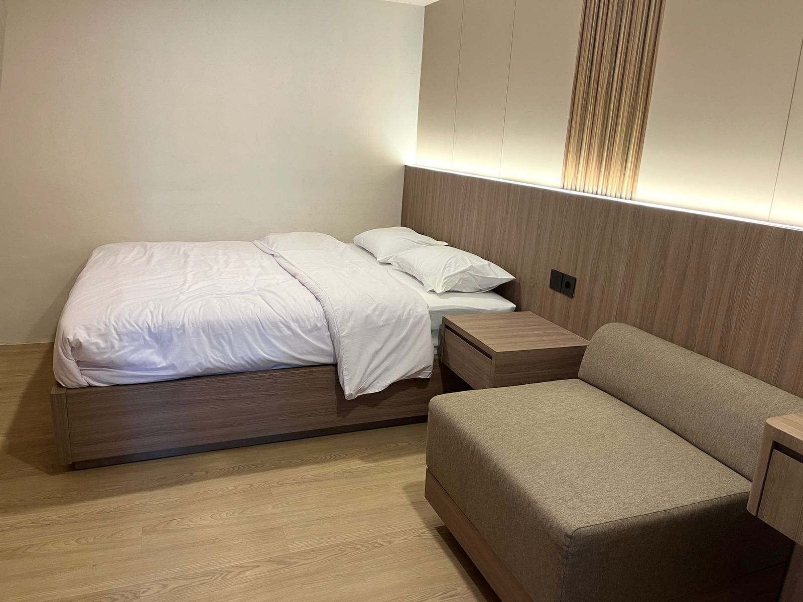 Quarto moderno com cama, mesas de cabeceira e um sofá.