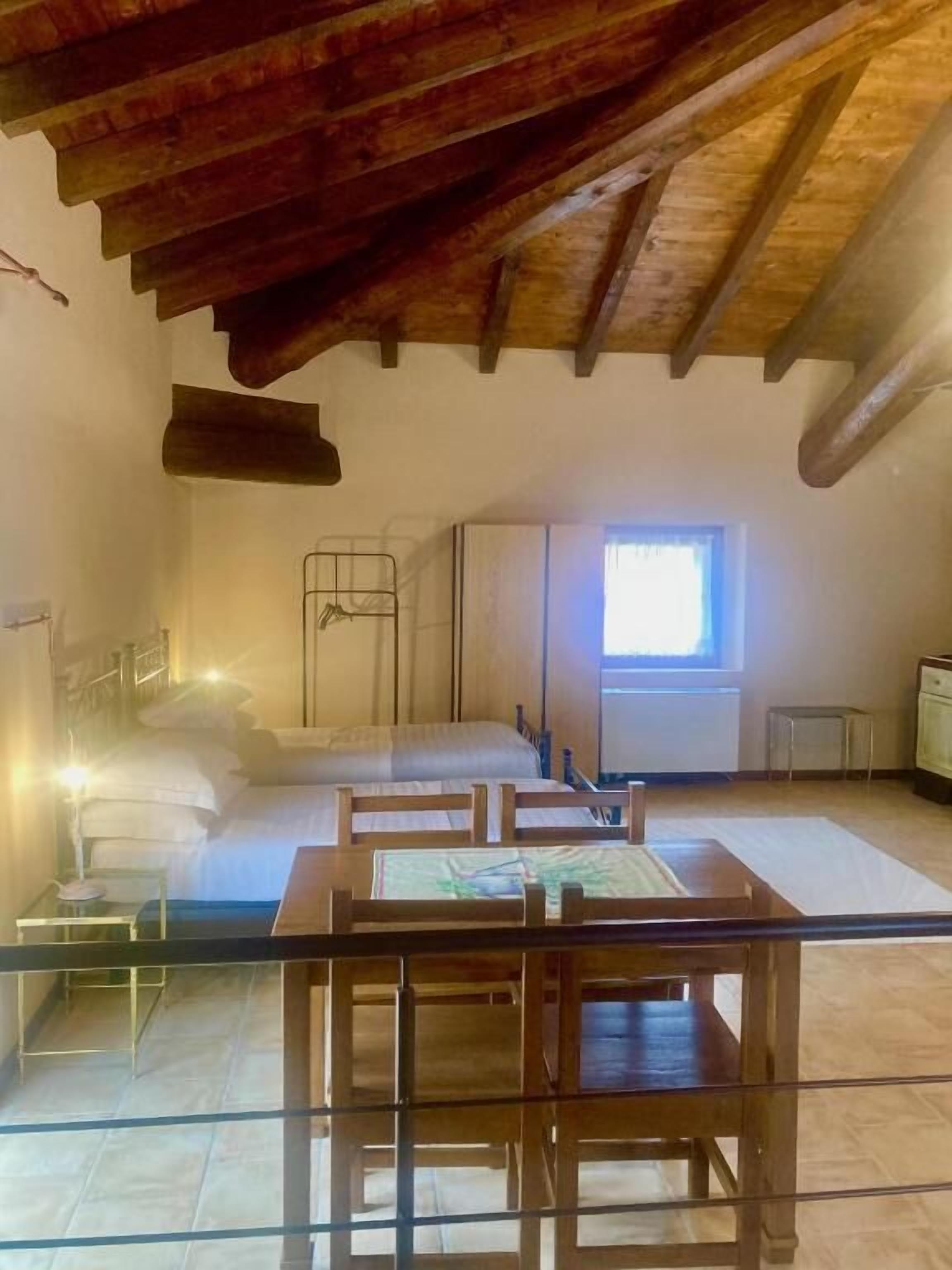 Um quarto de sótão aconchegante com teto de madeira, uma cama com roupa de cama branca, uma mesinha com um mapa e uma janela que deixa entrar luz natural.