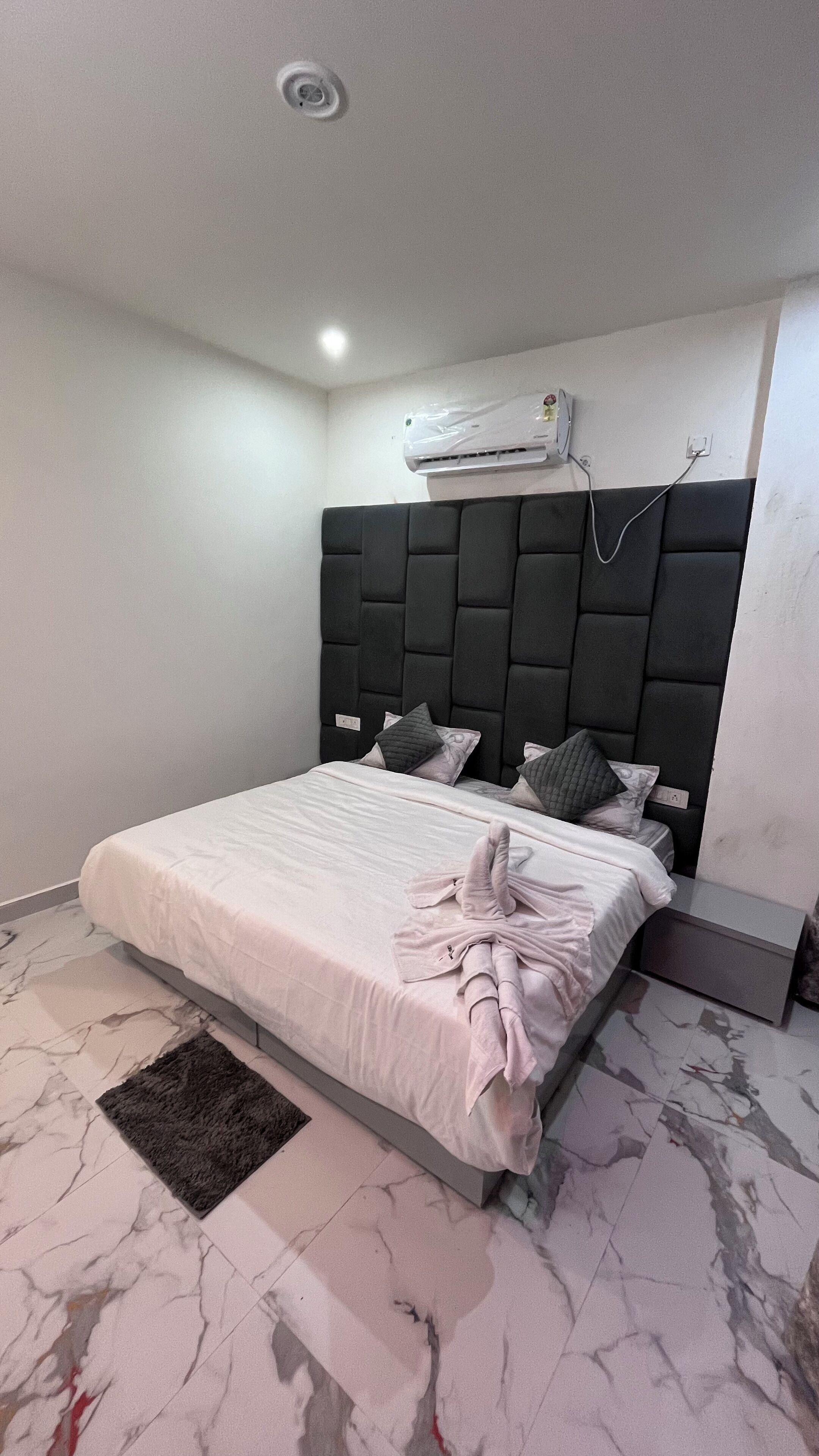 Quarto moderno com uma cama grande, cabeceira, aparelho de ar condicionado e piso de mármore.
