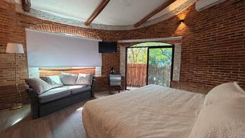 Quarto com cama, sofá, televisão e janela com vista para vegetação.