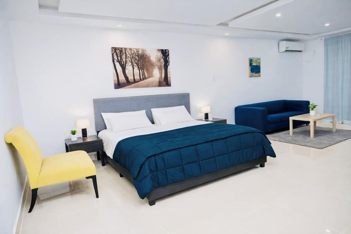 Quarto de hotel moderno com uma cama grande, um sofá, uma poltrona e uma mesinha.