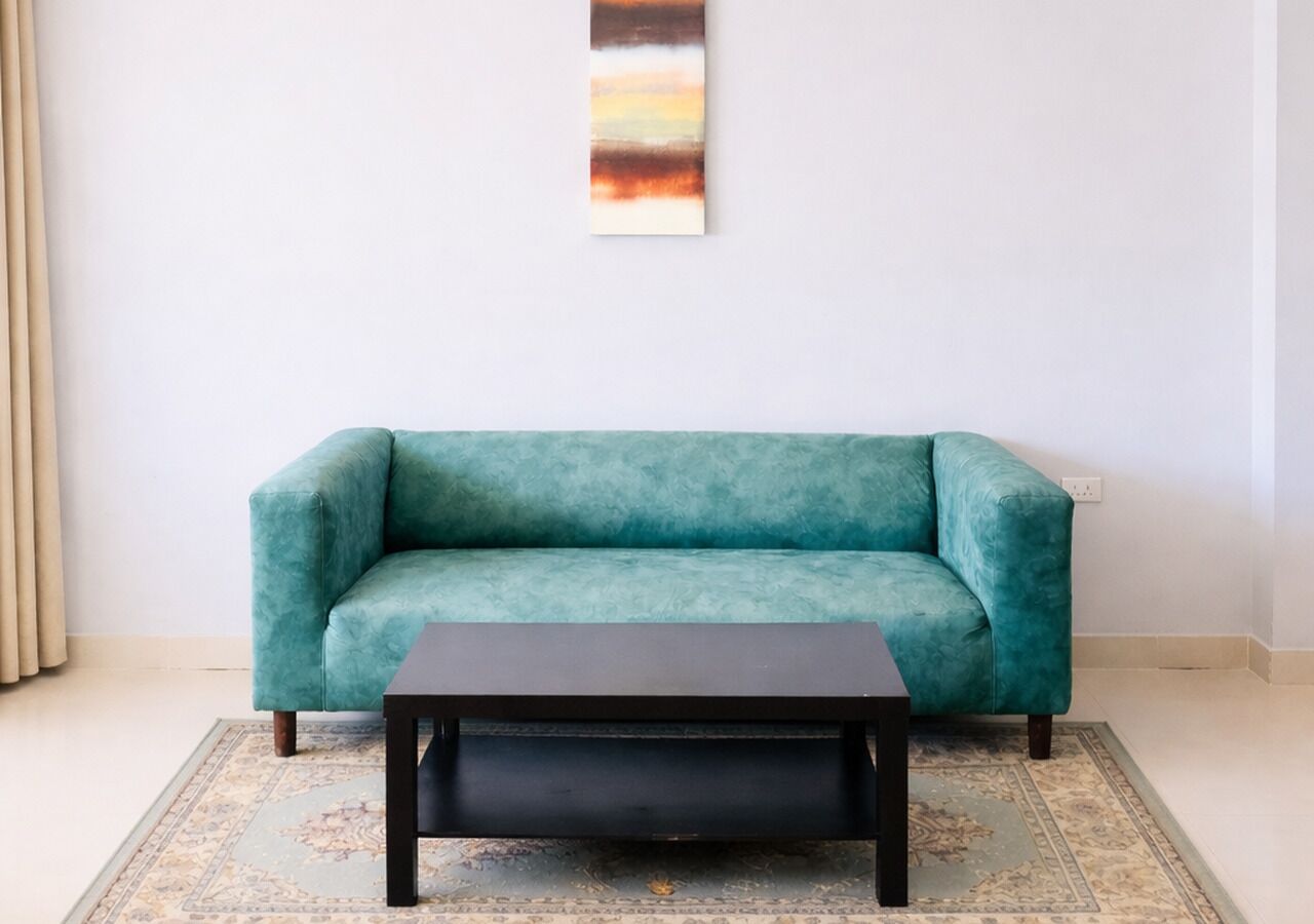Um sofá azul-turquesa e uma mesa de centro de madeira escura num quarto com um tapete estampado.