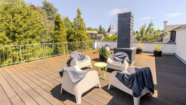 Terraço no telhado com área de estar ao ar livre, lareira e vegetação ao redor.
