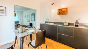 Cozinha moderna com área de refeições, destacando uma mesa de jantar cinza, cadeiras pretas, uma pequena mesa redonda com uma chaleira e um balcão preto com pia e armários.