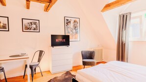 Quarto com cama, escrivaninha, cadeira, radiador e TV exibindo o logotipo da Netflix.