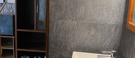 Casa de banho com lavatório branco, uma prateleira de madeira com sapatos, uma toalha e um telefone fixado na parede.