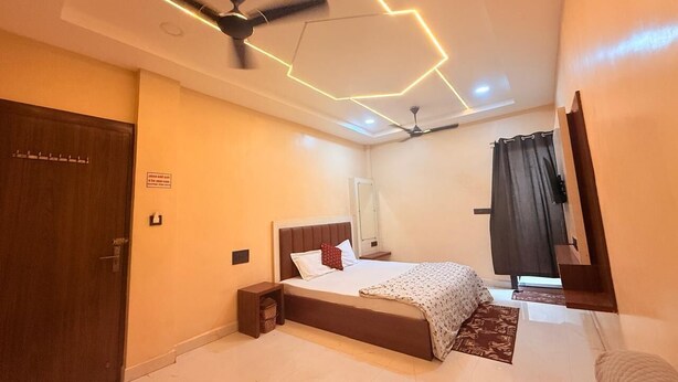 Quarto com cama, ventilador de teto, mesa de cabeceira, porta e janela com cortinas.