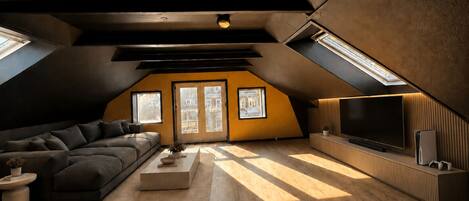 Um quarto moderno estilo loft com um sofá grande, uma televisão de tela plana e piso de madeira.