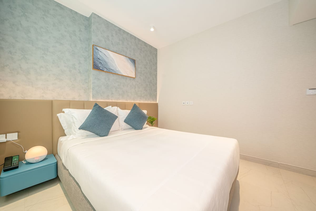 Quarto de hotel moderno com uma cama bem arrumada, uma luminária de cabeceira, um telefone em uma mesa de apoio e uma pintura pendurada na parede.