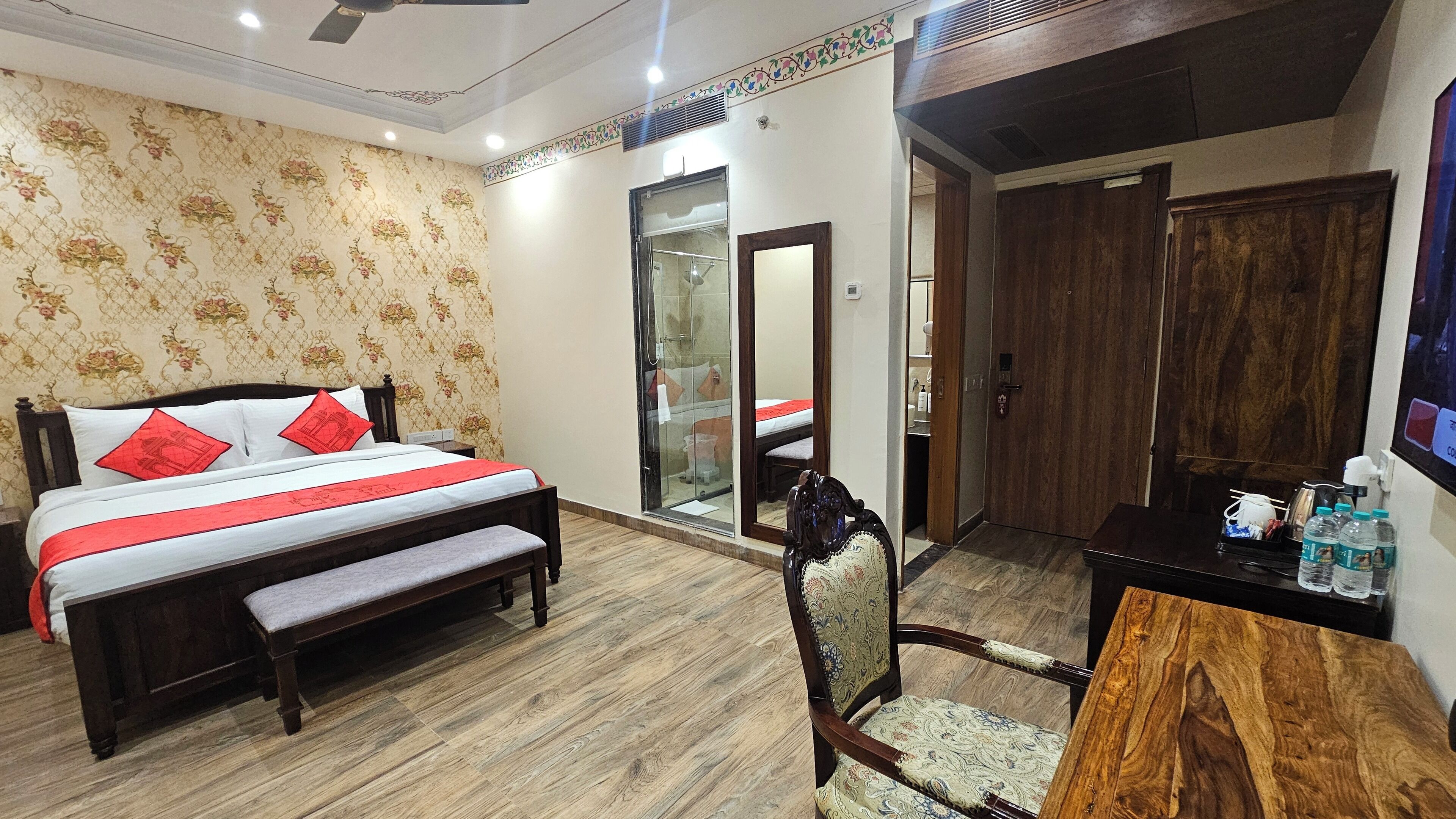 Quarto de hotel com uma cama, um banco de madeira, uma cadeira, uma escrivaninha e um guarda-roupa.