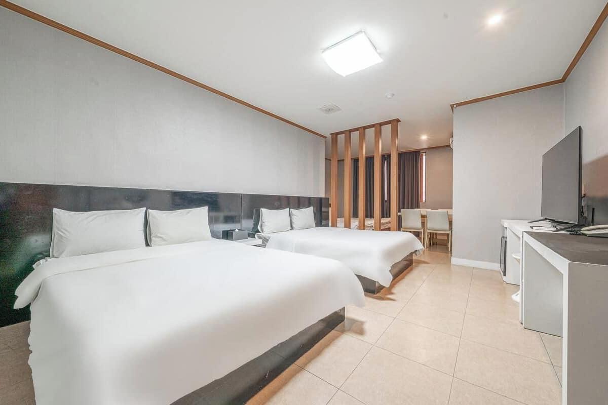 Quarto de hotel com duas camas, uma escrivaninha, televisão e janela.