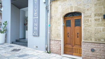 Entrada de hotel com fachada de pedra, porta dupla de madeira com puxadores de metal e placa indicativa do hotel boutique.