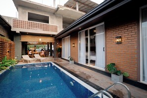 Piscina com espreguiçadeiras, área de refeições e parede externa de tijolos.