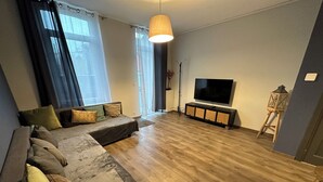 Uma sala de estar moderna com um sofá seccional, uma TV de tela plana e piso de madeira.