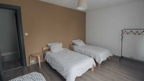 Quarto com duas camas de solteiro, uma mesinha e um cabideiro.