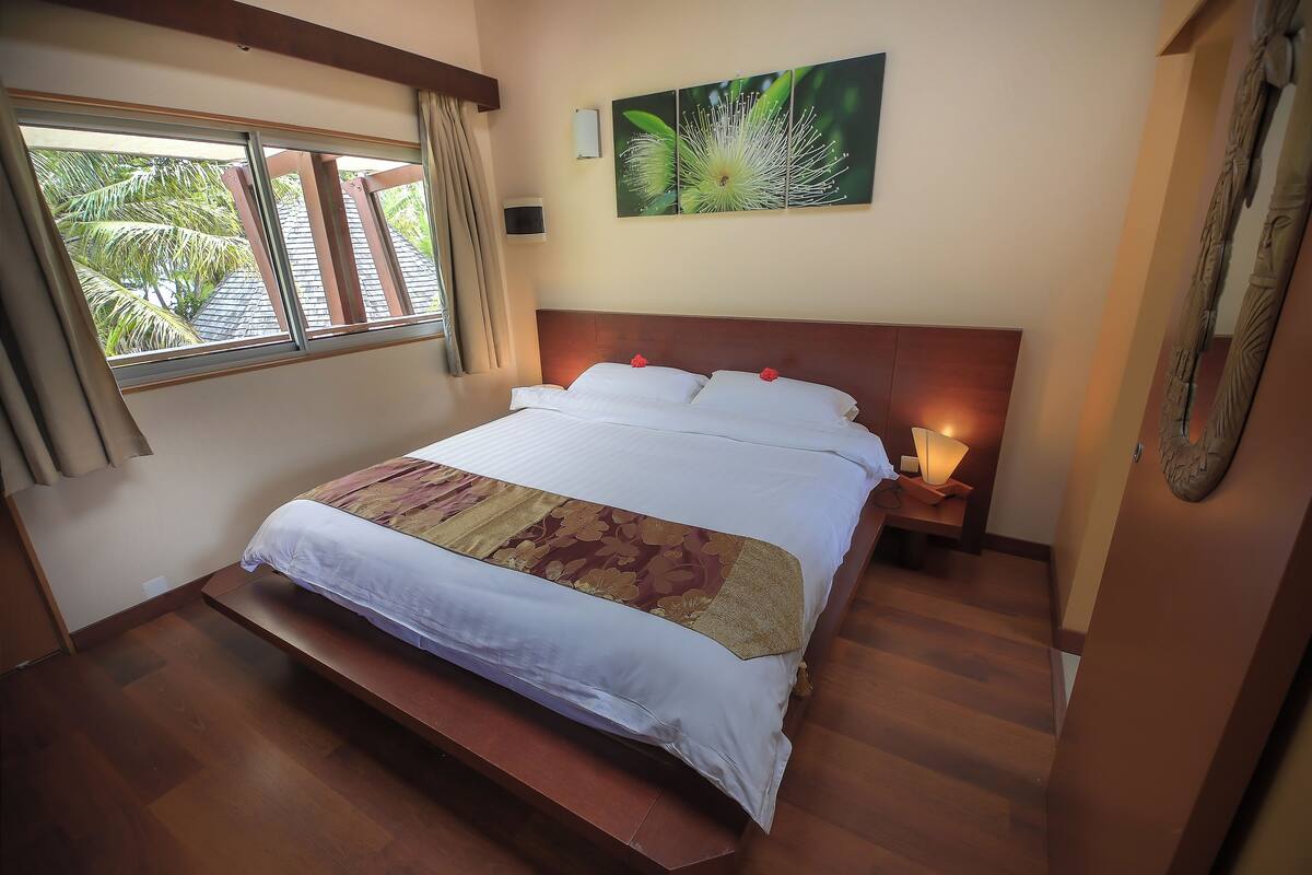 Uma cama bem arrumada com cabeceira de madeira, luminária de cabeceira e janela com cortinas.