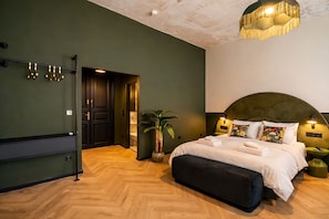 Quarto moderno com uma cama grande, um banco escuro, luminária pendente e uma planta em vaso.