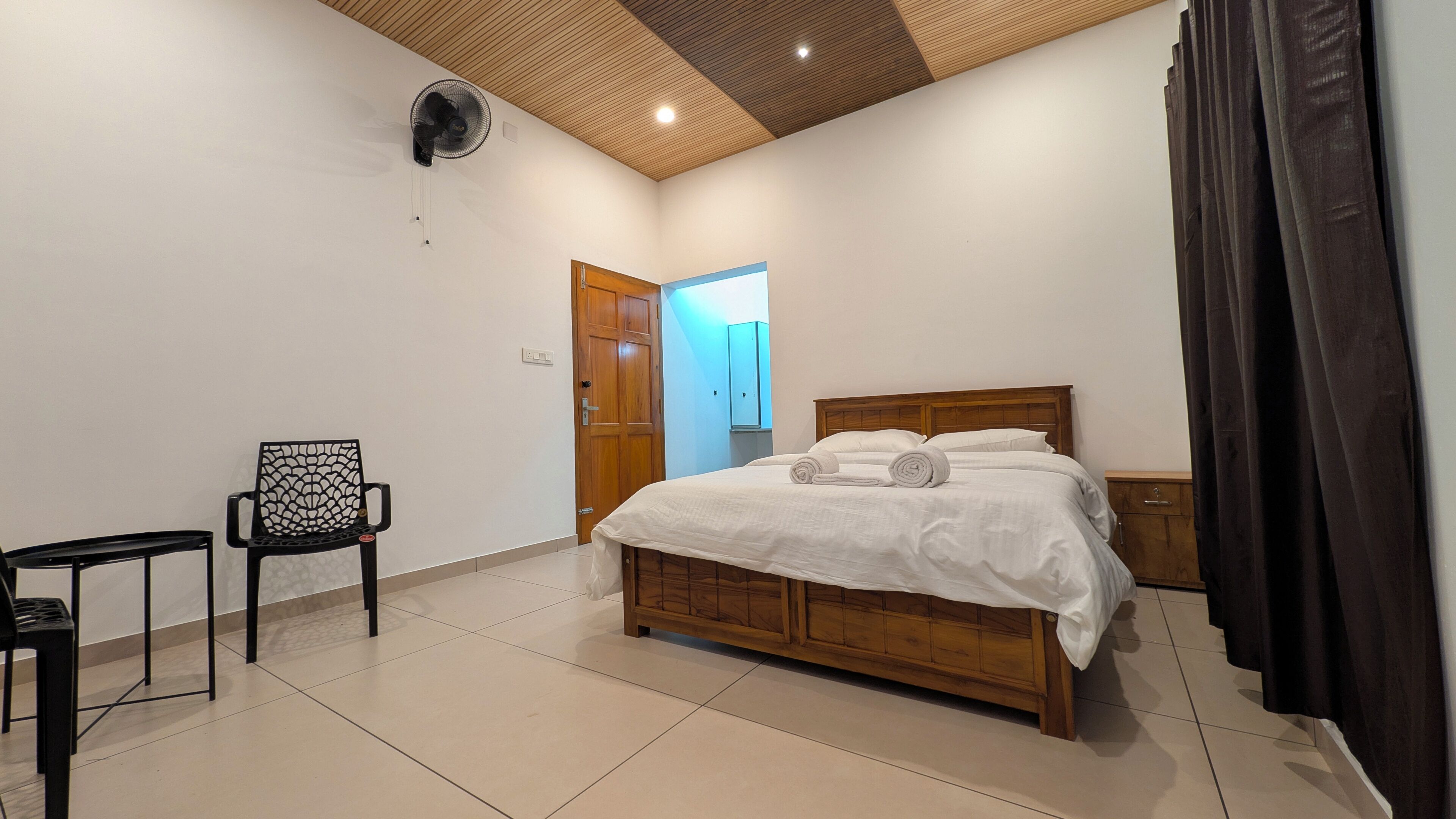 Quarto com cama de madeira, uma cadeira, mesa de cabeceira e ventilador de teto.