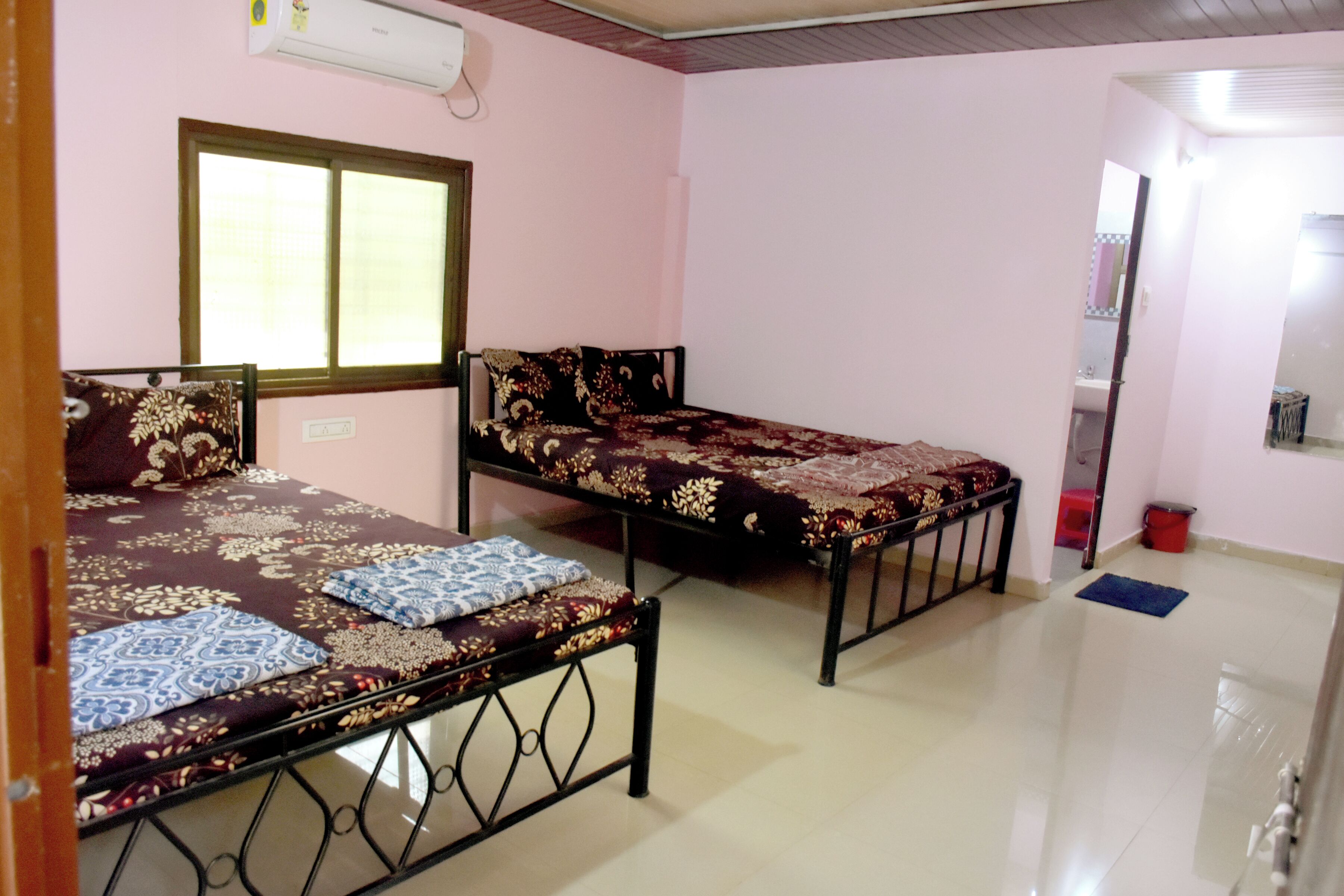 Quarto com duas camas, cada uma com roupa de cama estampada, uma janela e uma porta que dá para outro quarto.