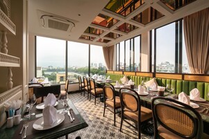 Um restaurante com vista para a cidade, com assentos estofados em verde e chão estampado.