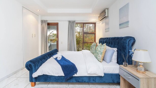Quarto com uma cama grande, uma mesa de cabeceira, uma luminária e uma janela com cortinas.