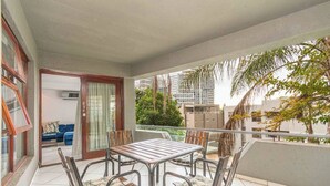 Varanda com mesa e cadeiras, vista para a cidade e porta que dá para um espaço interno.