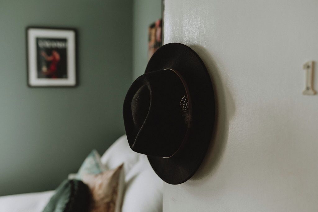 Quarto com uma cama, um chapéu fixado na parede e um quadro emoldurado.