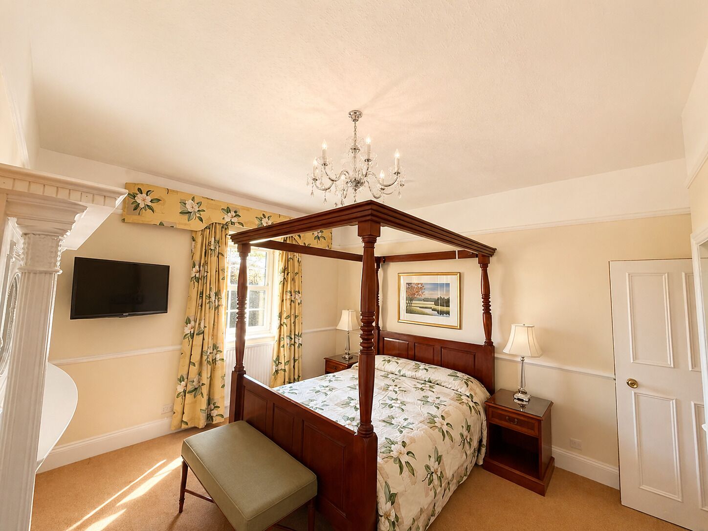 Quarto com cama de dossel, lustre, televisão, mesa de cabeceira com abajur e janela com cortinas.