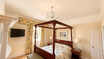 Quarto com cama de dossel, lustre, televisão, mesa de cabeceira com abajur e janela com cortinas.
