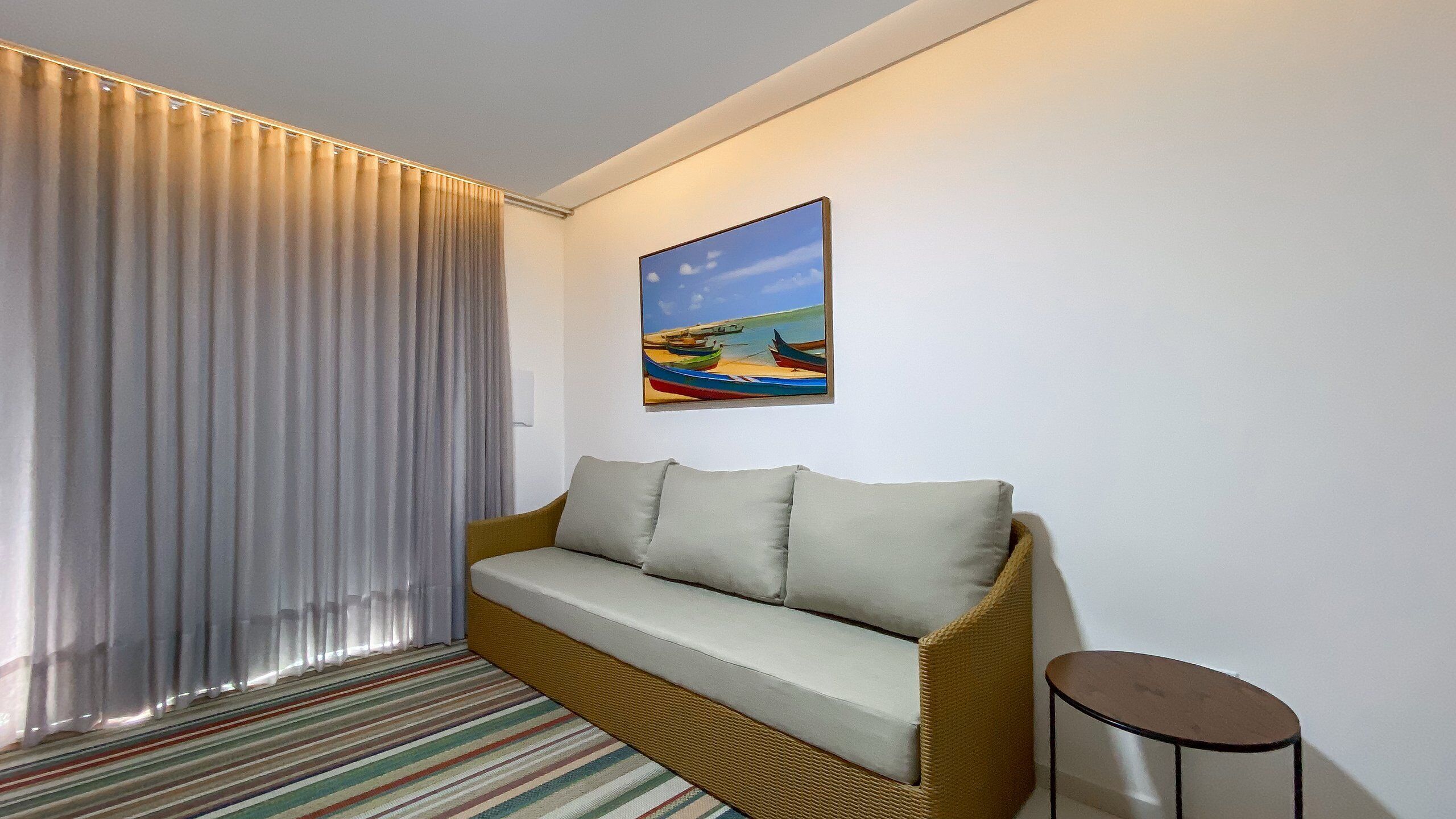 Quarto com sofá, um quadro, tapete listrado e uma pequena mesa.