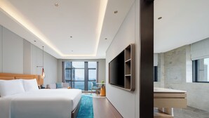 Quarto de hotel moderno com uma cama grande, televisão, escrivaninha e vista para a cidade.
