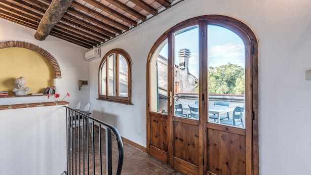 Quarto com teto de madeira, parede branca com arco amarelo e porta de madeira grande com painéis de vidro.