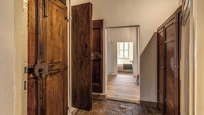 Um corredor com portas de madeira, chão de pedra e vista para um quarto com cama e janela.