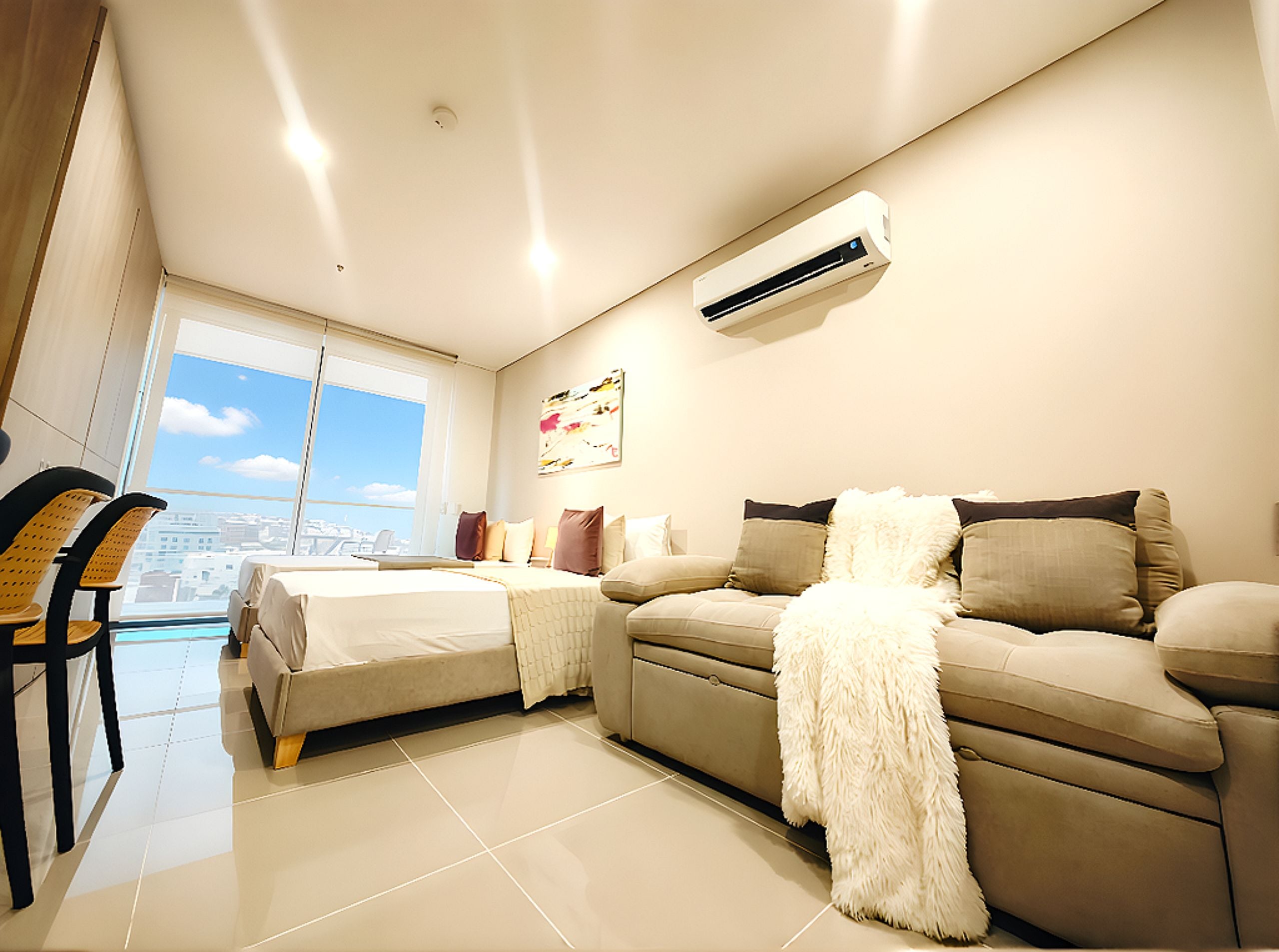 Quarto de hotel moderno com cama, sofá e vista para a cidade.