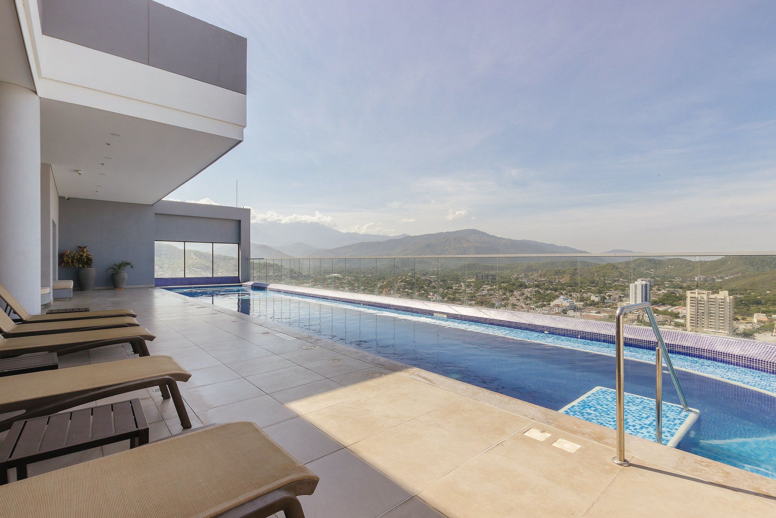 Piscina no terraço com espreguiçadeiras, vista para montanhas e paisagem urbana ao fundo.