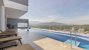 Piscina no terraço com espreguiçadeiras, vista para montanhas e paisagem urbana ao fundo.