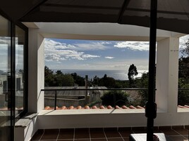 Uma varanda com vista para o mar, chão de azulejos e guarda-corpo.