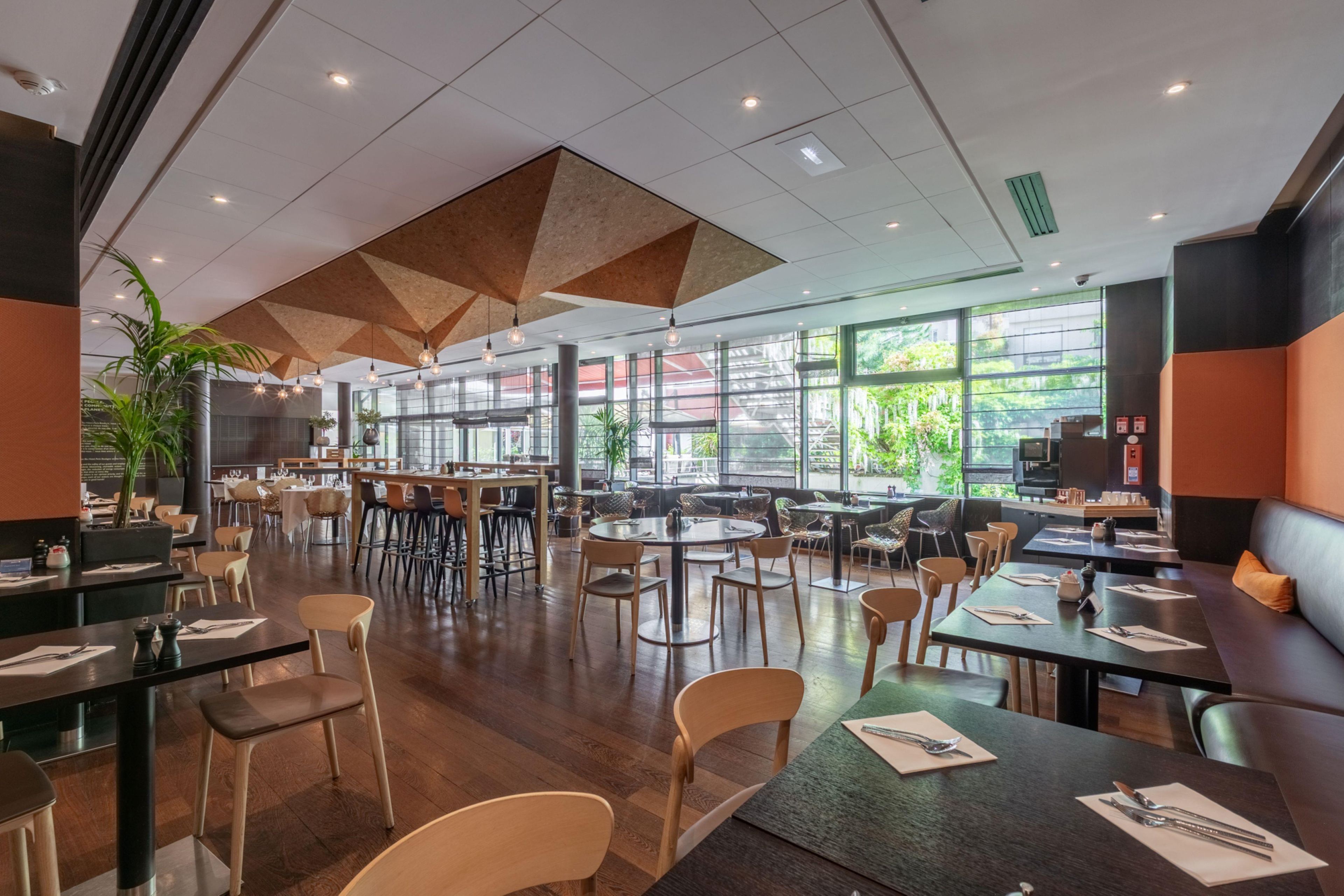 Um restaurante amplo, com pé-direito alto, grandes janelas e diversos tipos de assentos.