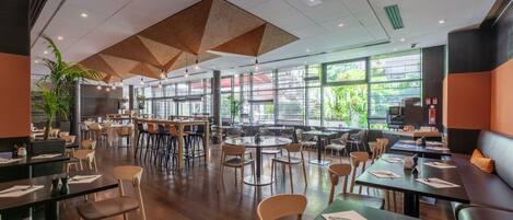 Um restaurante amplo, com pé-direito alto, grandes janelas e diversos tipos de assentos.