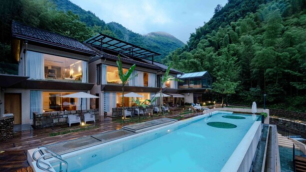 Um hotel moderno com uma piscina grande, área de estar ao ar livre e vista para uma montanha arborizada.